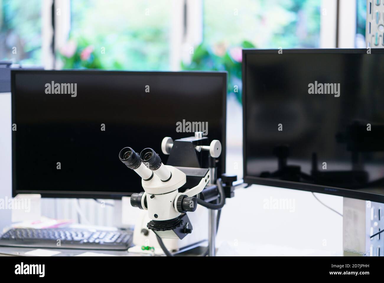 White microscope against computer monitors at illuminated laboratory ...