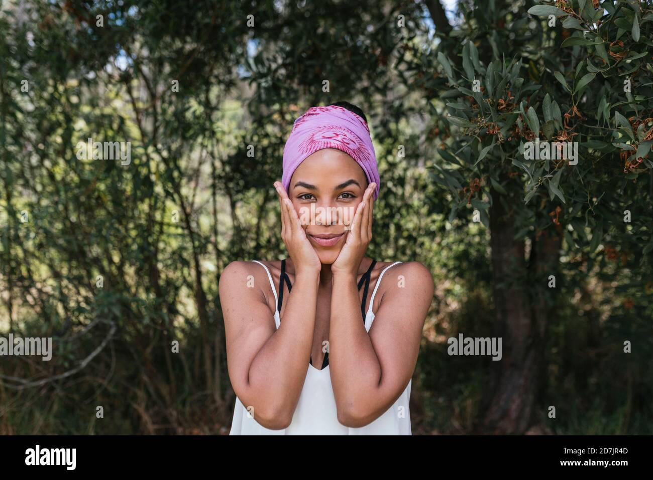 Young woman with hands on cheeks wearing purple bandana while standing ...