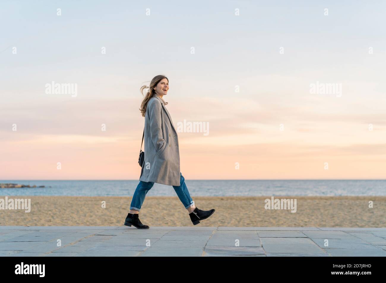 Happy beautiful woman walking on promenade at beach while looking away ...