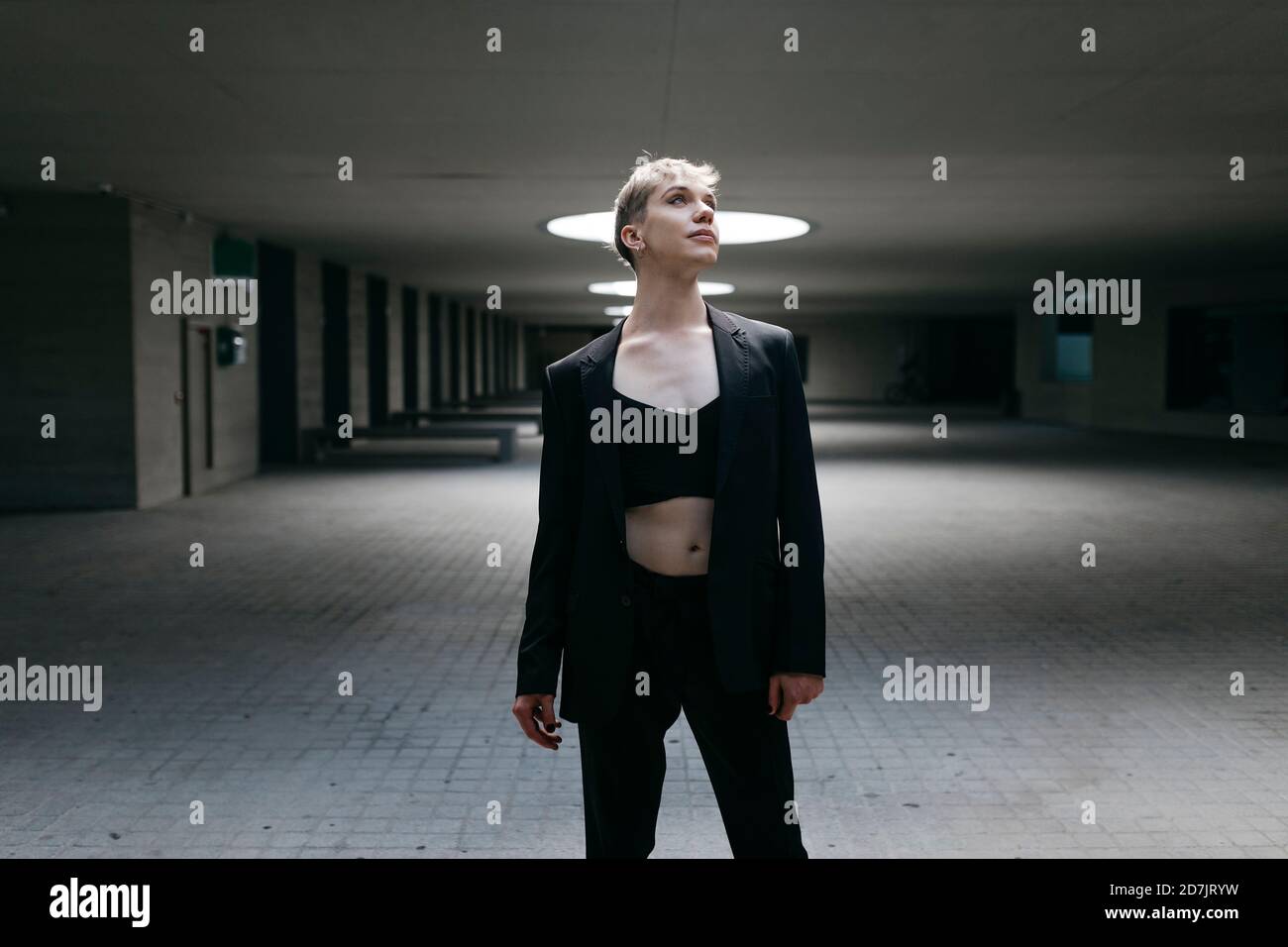 Thoughtful trans young man wearing black suit standing on floor in ...