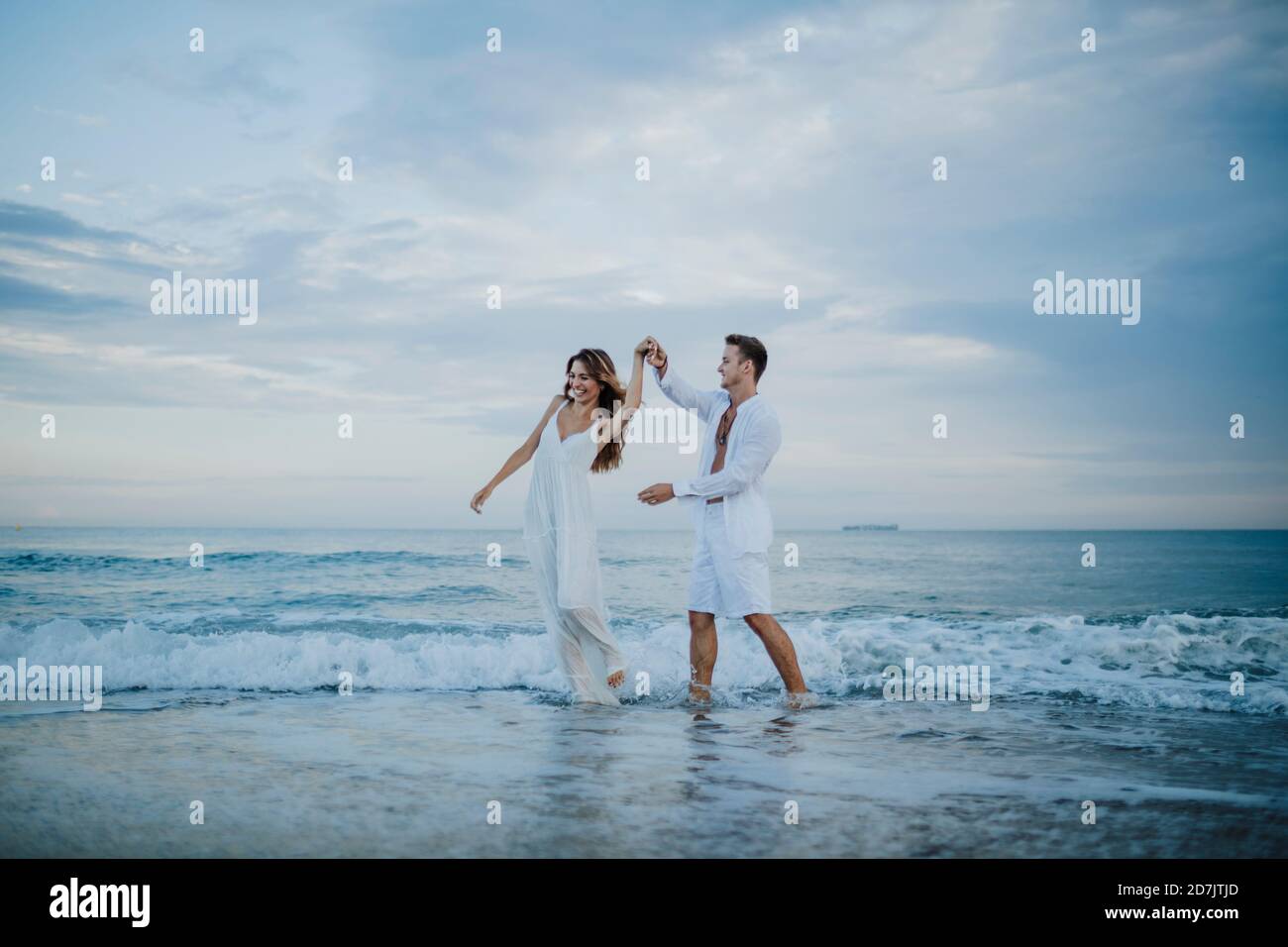 Young couple spinning woman while dancing in water at beach Stock Photo ...