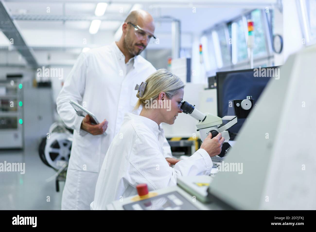 Male technician standing by female scientist looking into microscope ...