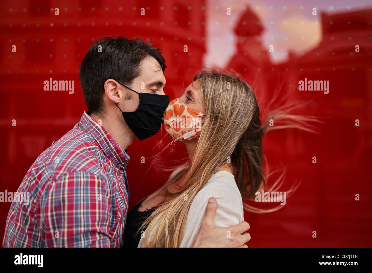 Couple kissing with protective face mask standing against acrylic wall ...