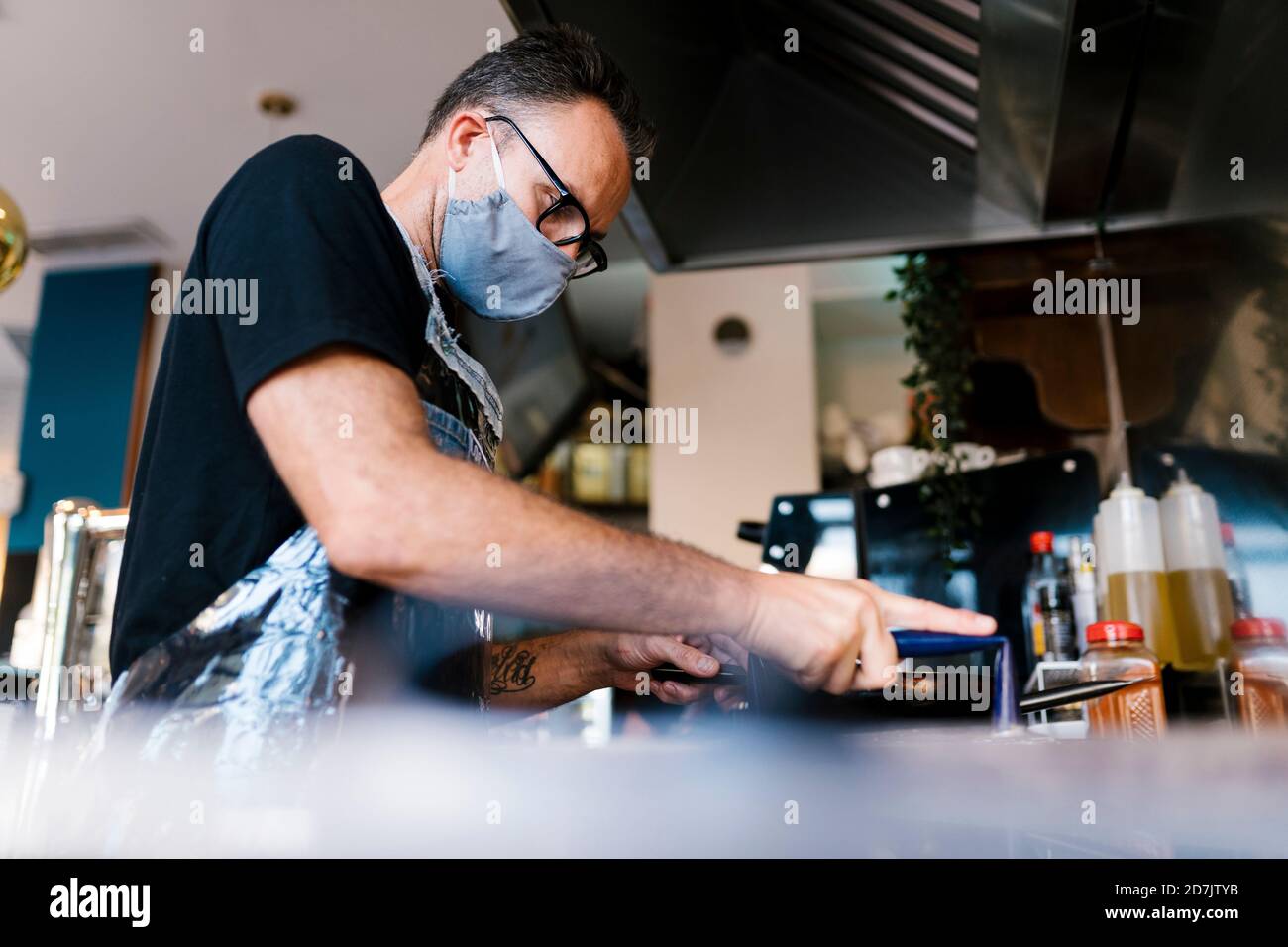 Male barista wearing face mask while cooking in kitchen of coffee shop ...