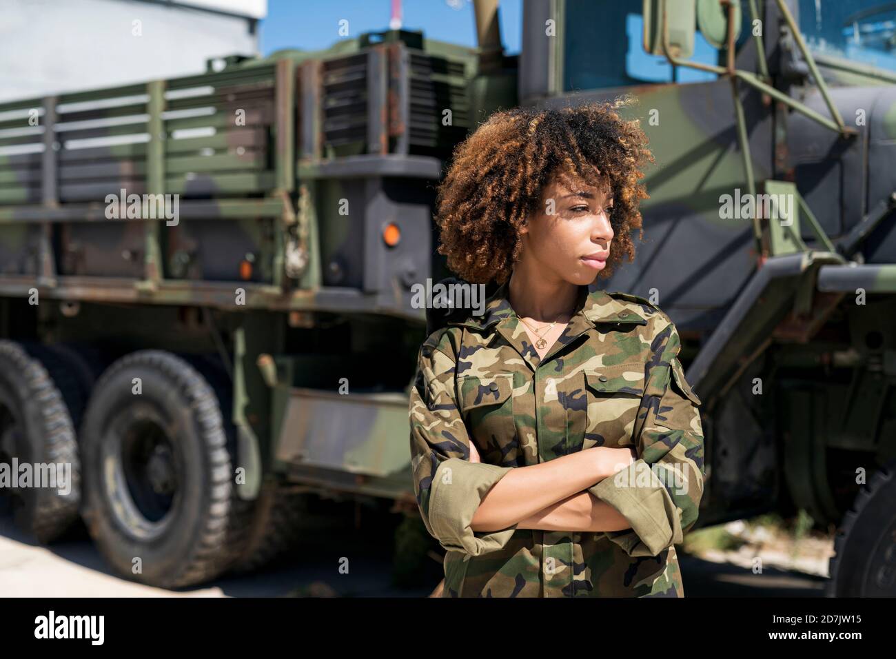 Young female army soldier with arms crossed looking away while standing ...