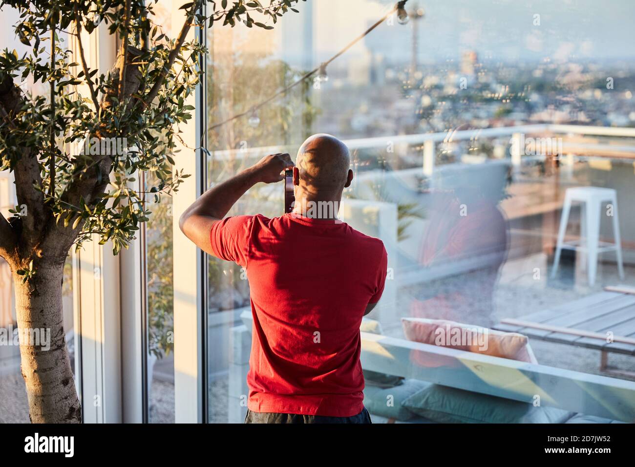 Mature man photographing sunset through window at rooftop Stock Photo ...