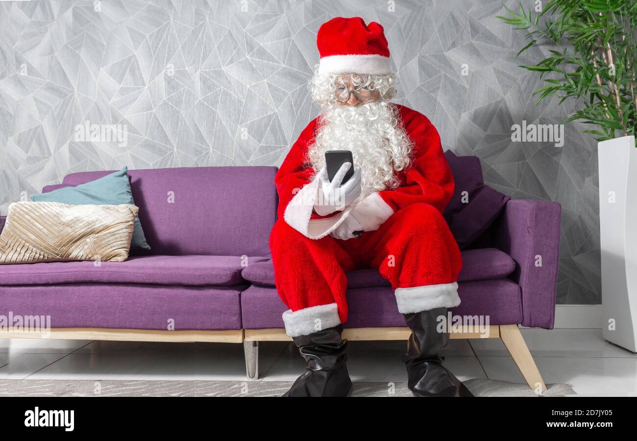 Santa Claus at Christmas sitting on a couch checking his cell phone ...
