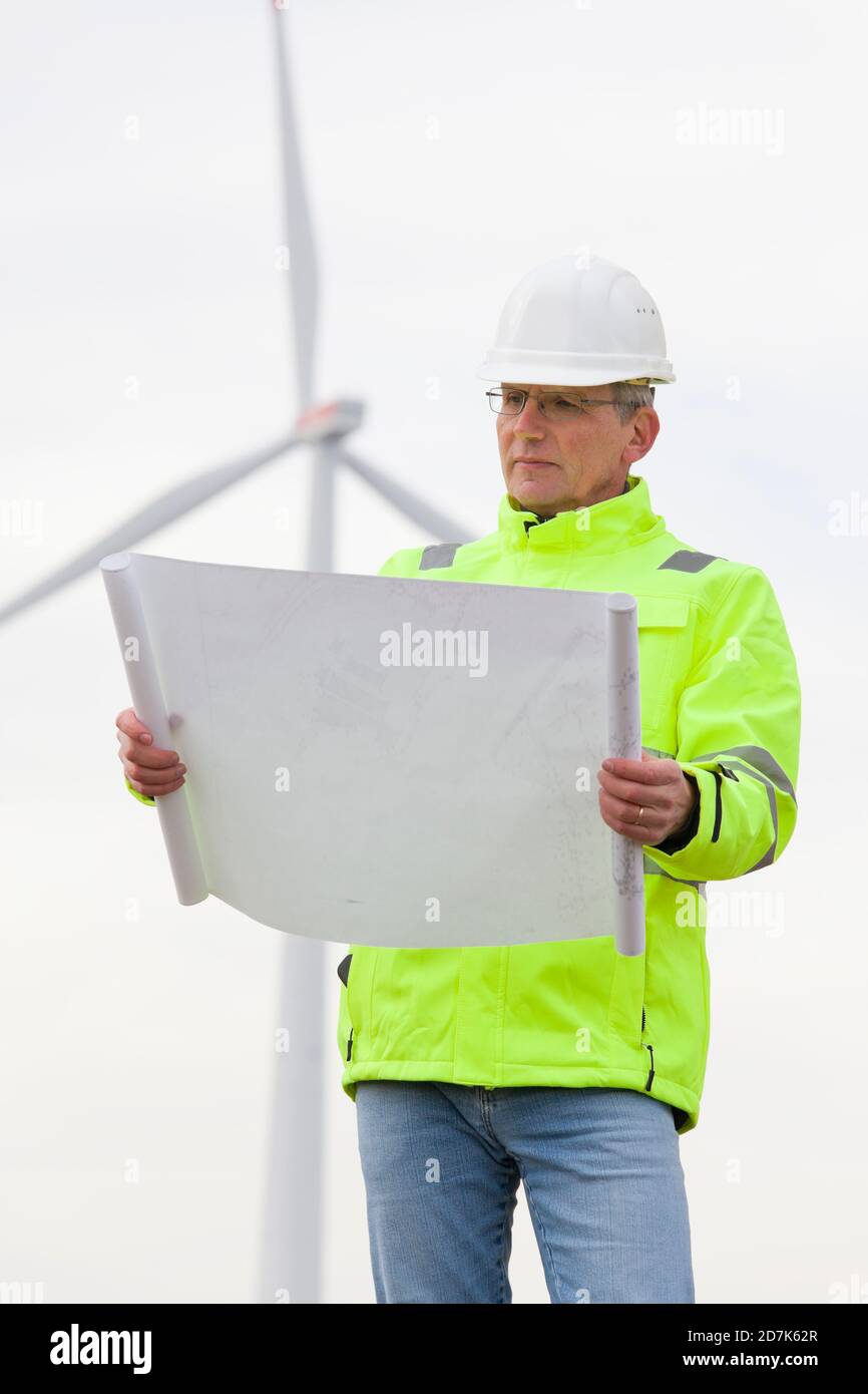 Mature engineer standing in front of a wind turbine with blueprint in ...