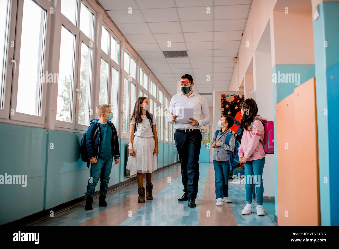 Elementary school students and male teacher wearing protective face ...