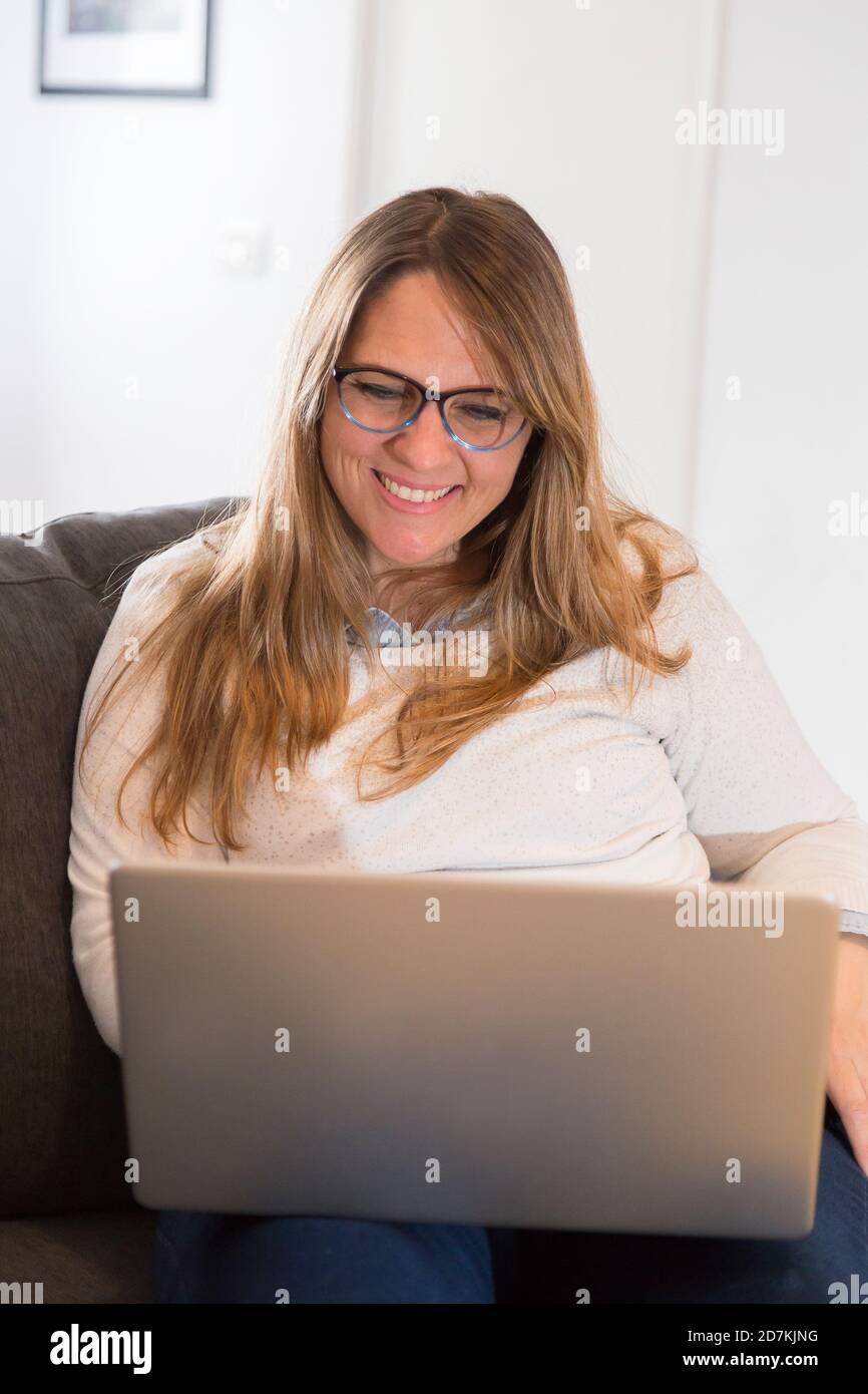 Woman at home with a laptop. She is sitting in an sofa with a computer ...