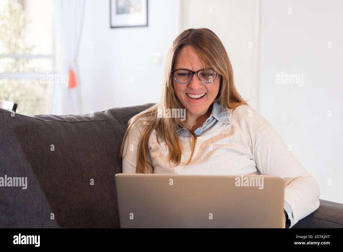 Woman at home with a laptop. She is sitting in an sofa with a computer ...
