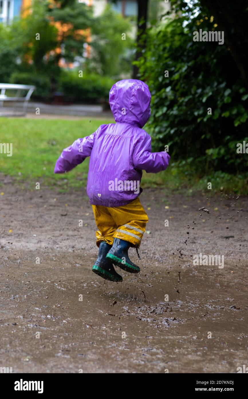 Child from behind jumping into a puddle of mud during a rainy and wet ...