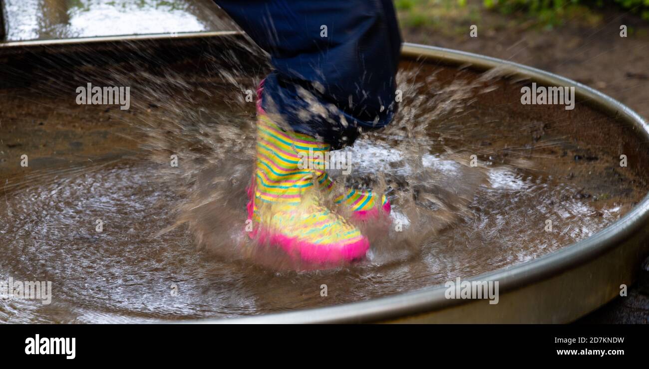 Detail of colorful rubber boots of a child jumping into a puddle of mud ...