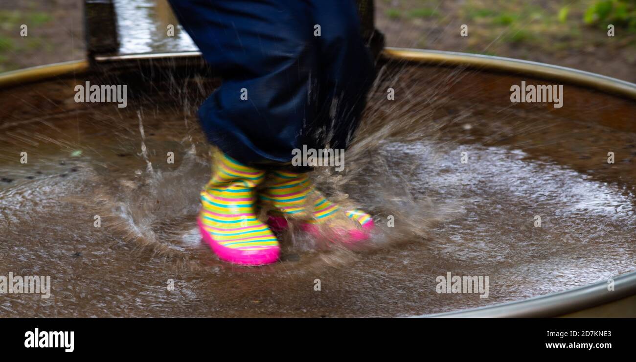 Detail of colorful rubber boots of a child jumping into a puddle of mud ...