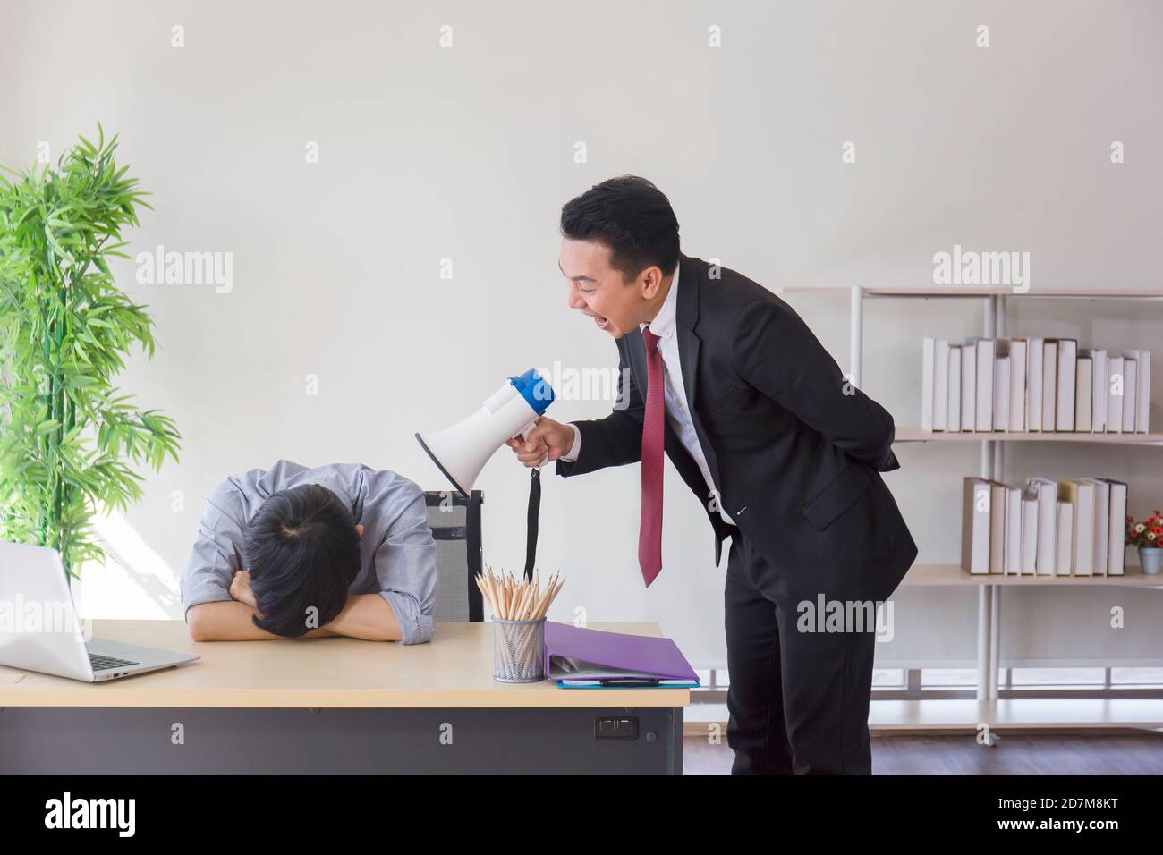An Asian male supervisor uses a megaphone to shout at his sleeping ...