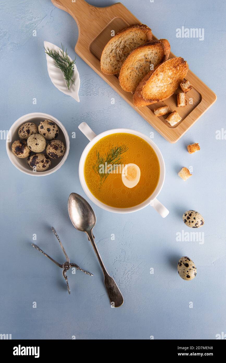 Bouillon, quail egg and fennel leaf in white soup bowl on blue ...