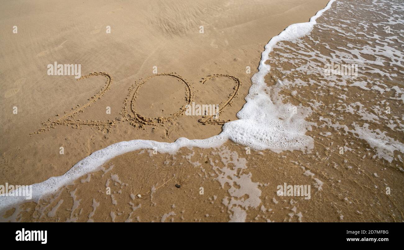 the year 2020 in tet written in sand on beach is covered by ocean wave ...