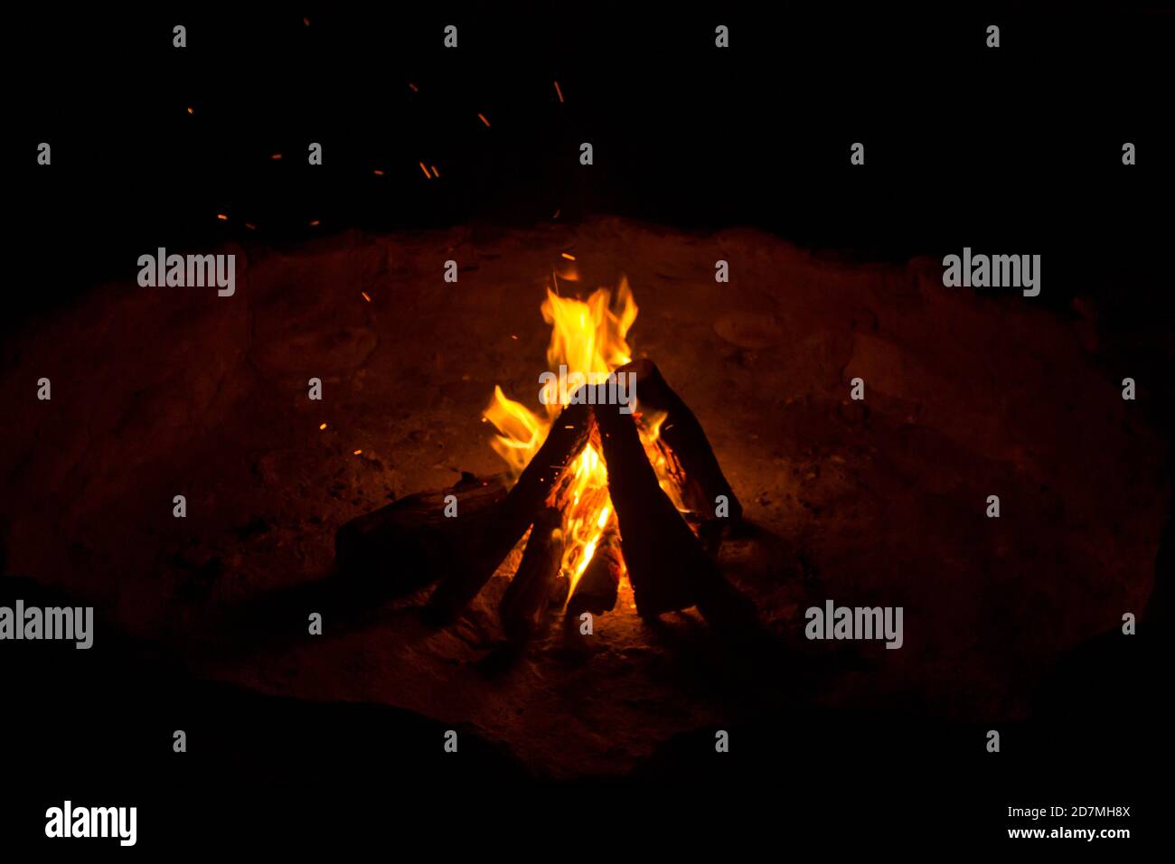 A wood fire burning in a wide outdoors fire pit outside during night ...