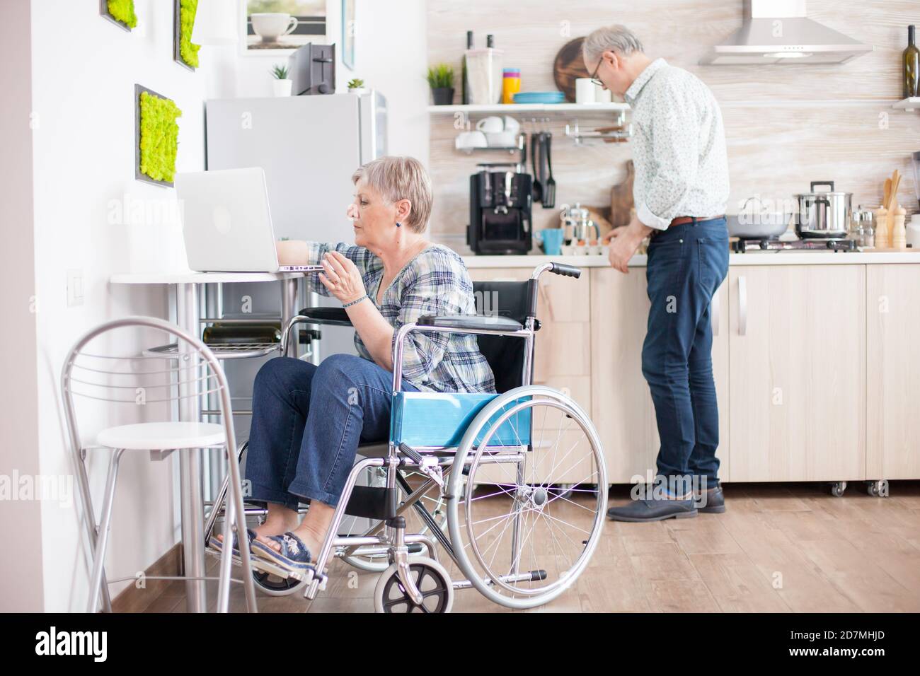 Disabled old woman in wheelchair working on laptop in kitchen ...