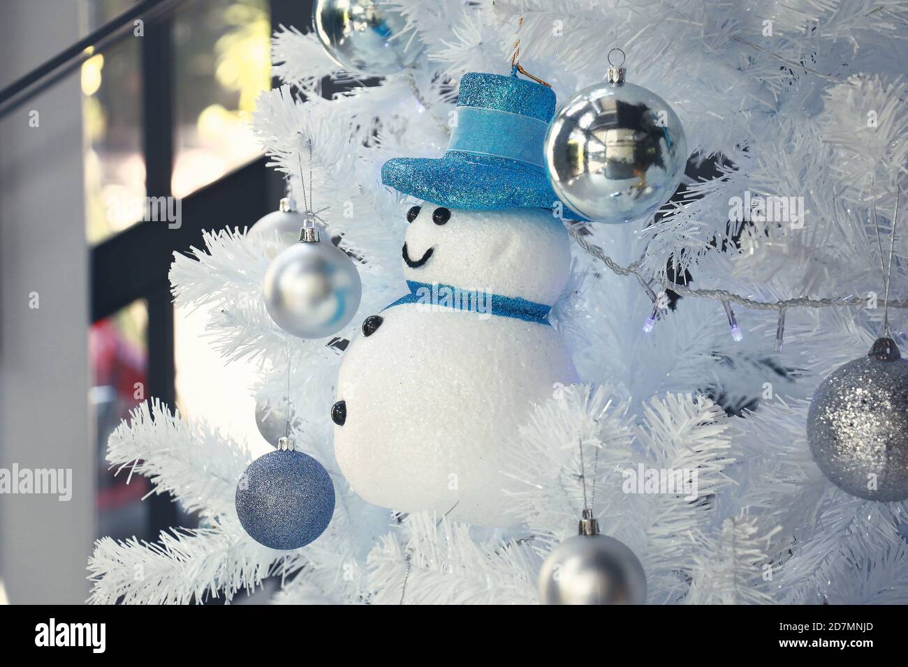 a blue snowman toy and many silver balls are hanging on white chrismas ...