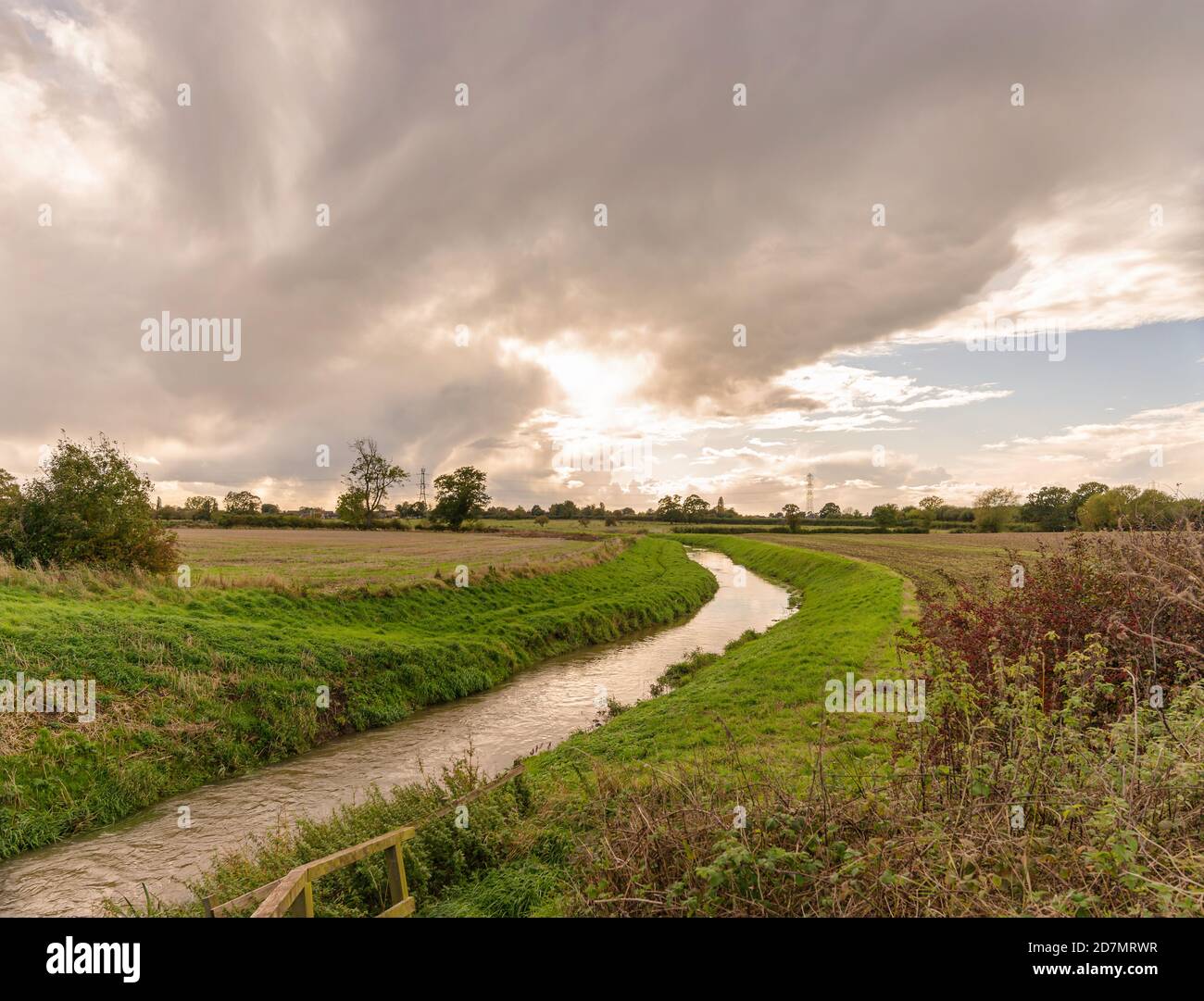A small river curves between two fields that have been ploughed after ...