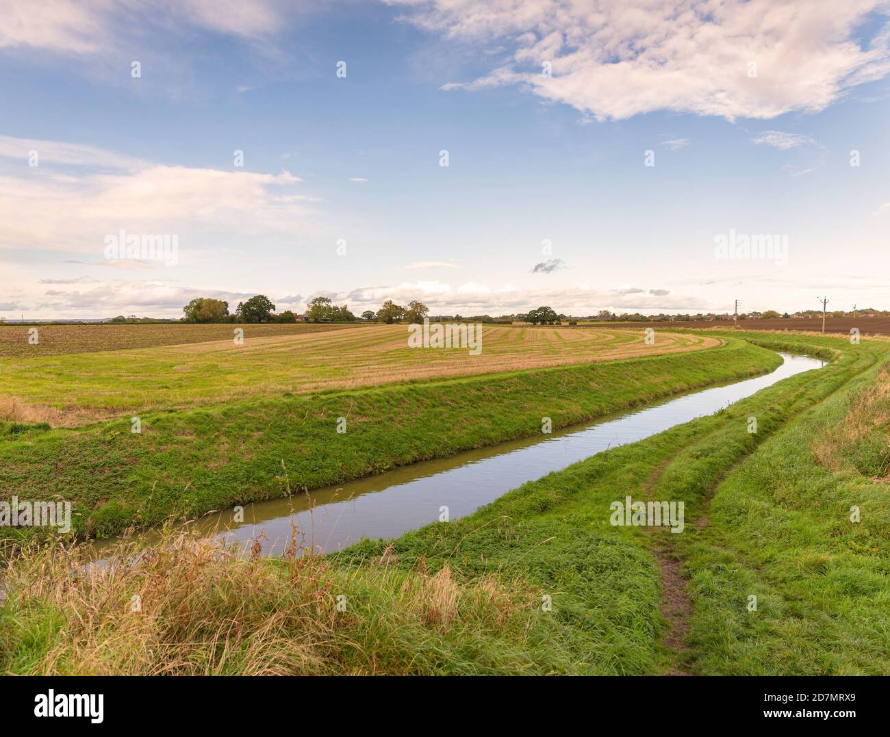 A stream curves alongside a field with lines made by a tractor. There ...