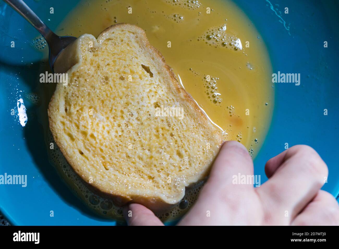 Hands dipping a slice of bread in beaten egg on a blue plate to make ...