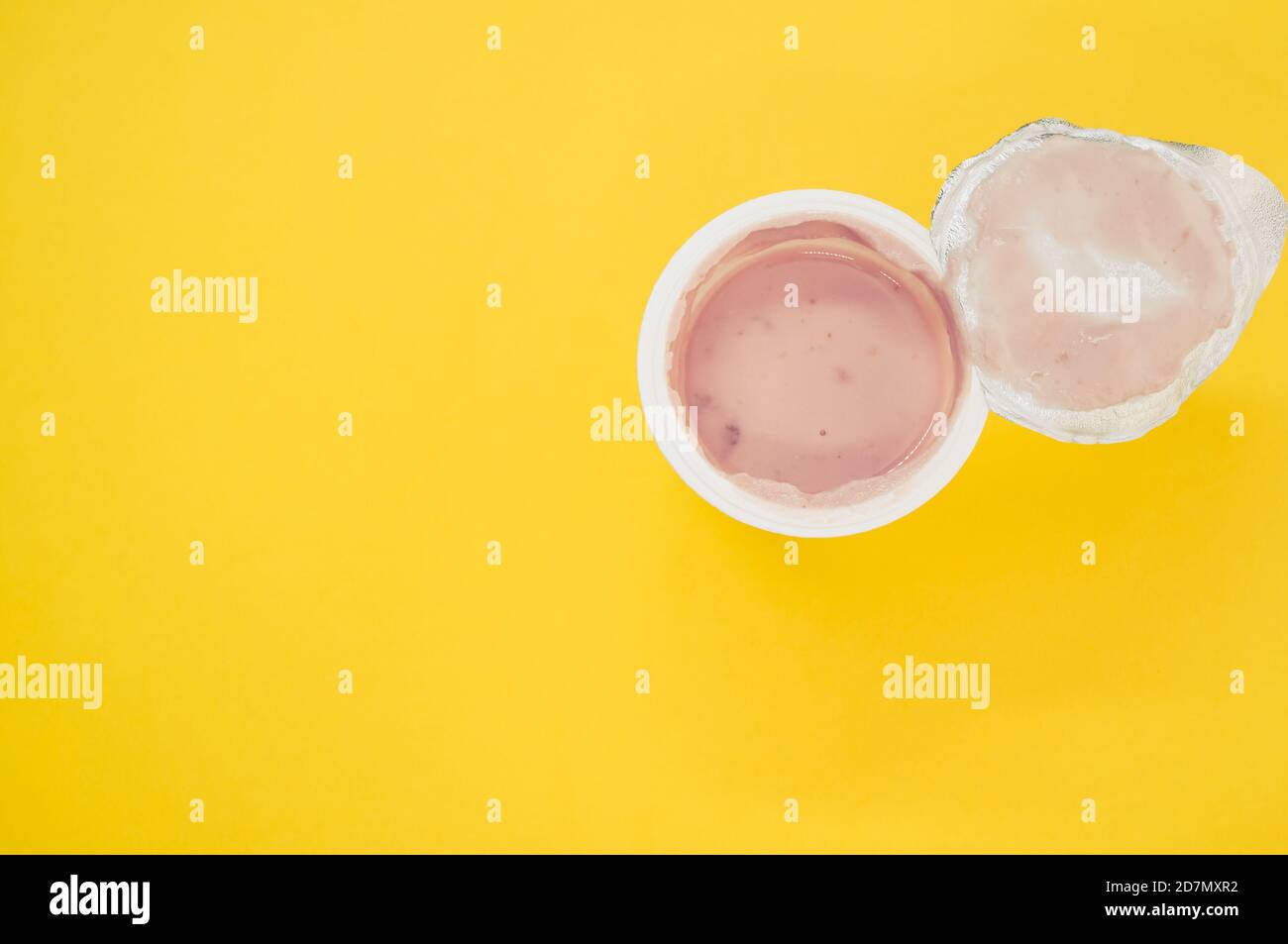 Top view of an opened plastic container of fruit yogurt on a yellow ...