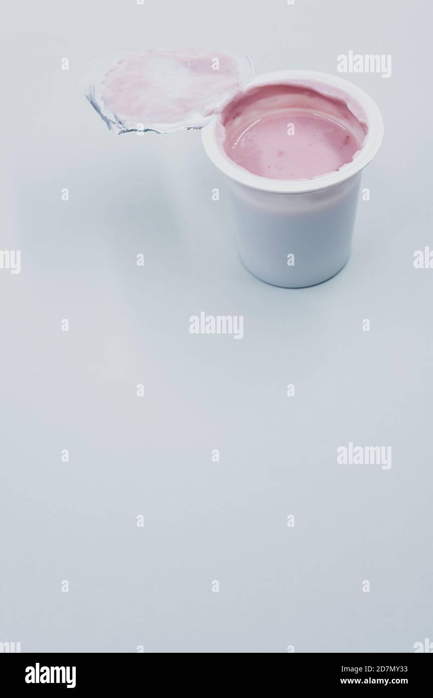 Vertical shot of an opened plastic container of fruit yogurt on a white ...