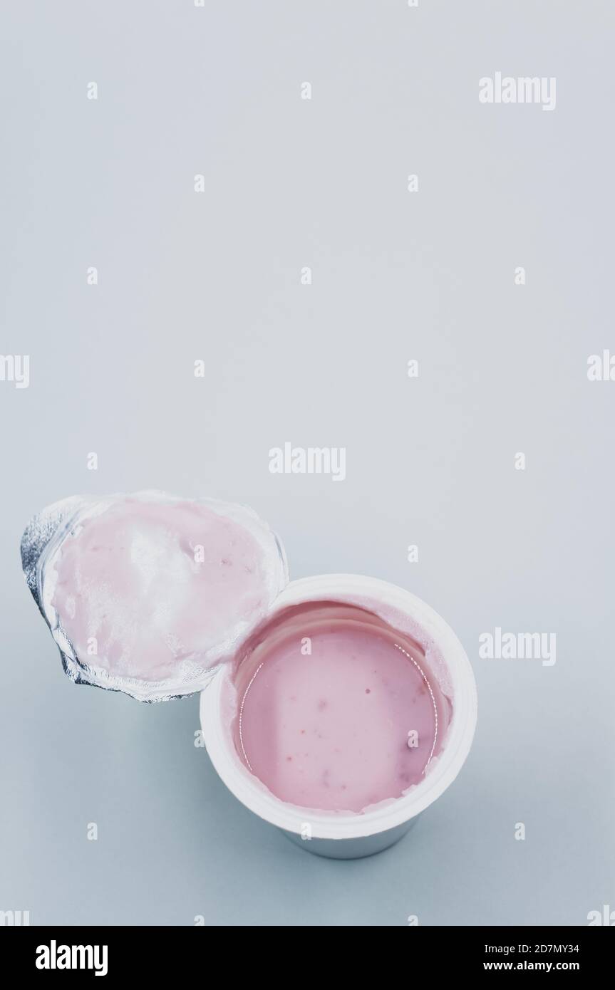 Vertical shot of an opened plastic container of fruit yogurt on a white ...