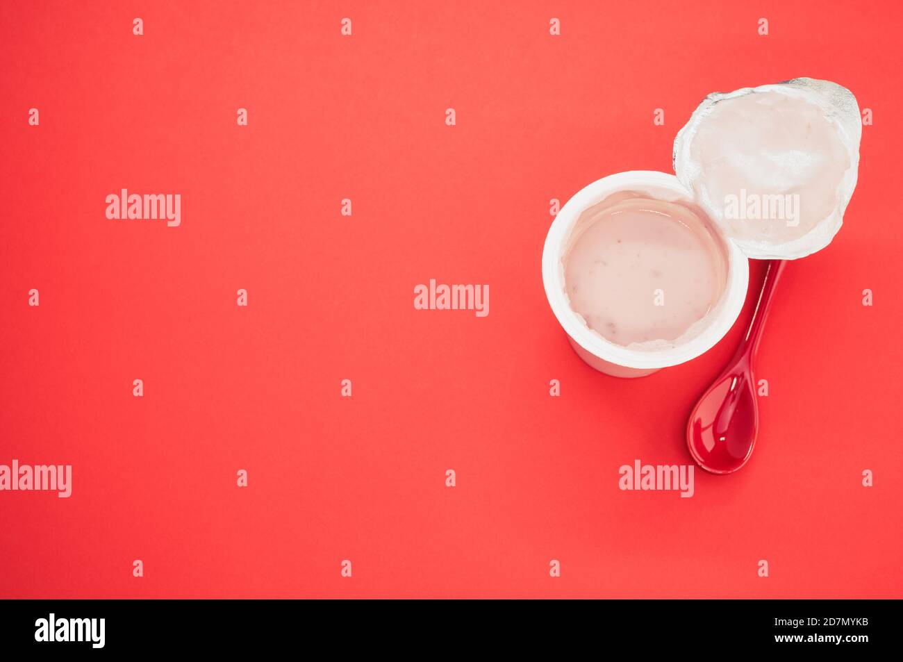 Top view of an opened plastic container of fruit yogurt and a spoon, on ...