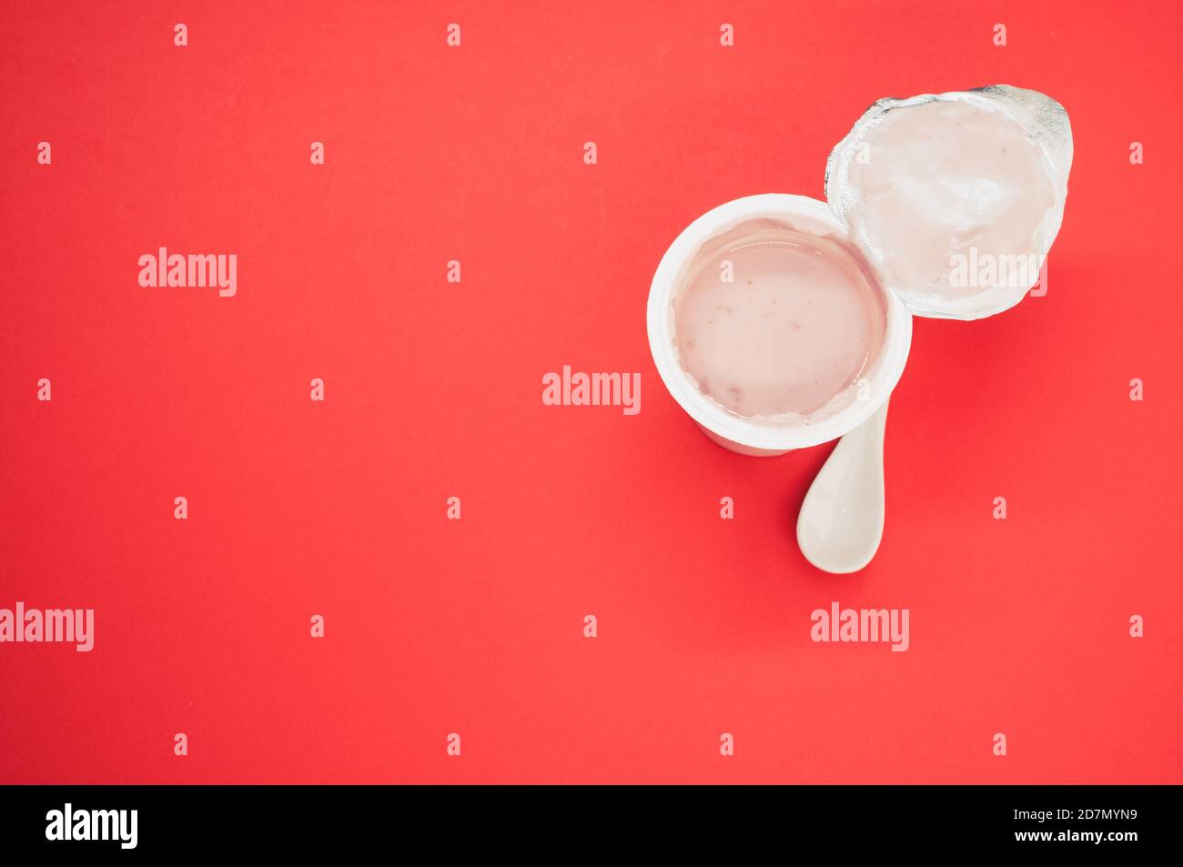 Top view of an opened plastic container of fruit yogurt and a spoon, on ...