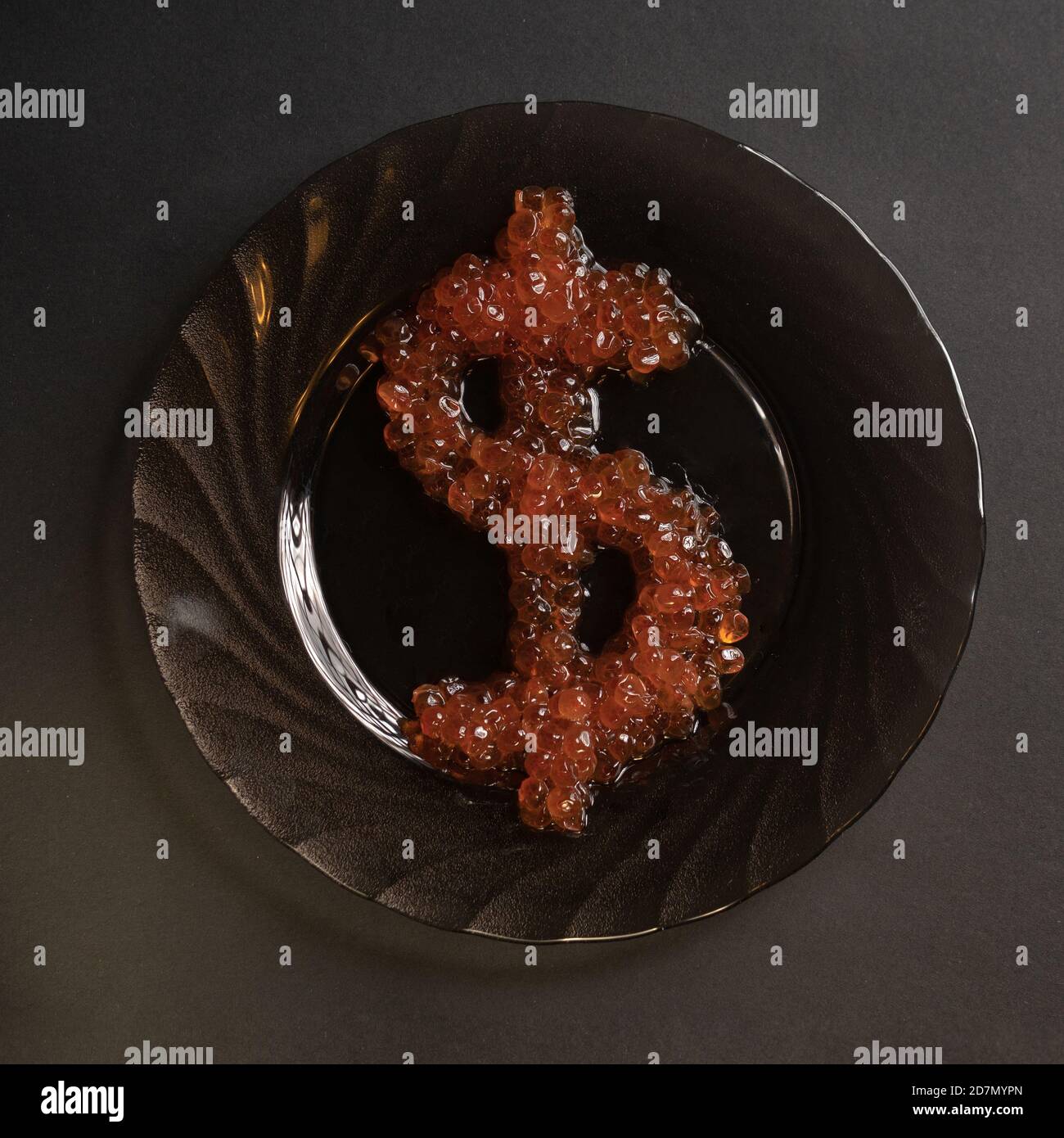 The symbol of a dollar of red caviar on a black plate on a gray ...
