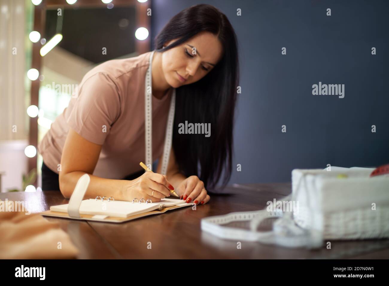 Beautiful young woman designer is making notes of clothing measurements ...