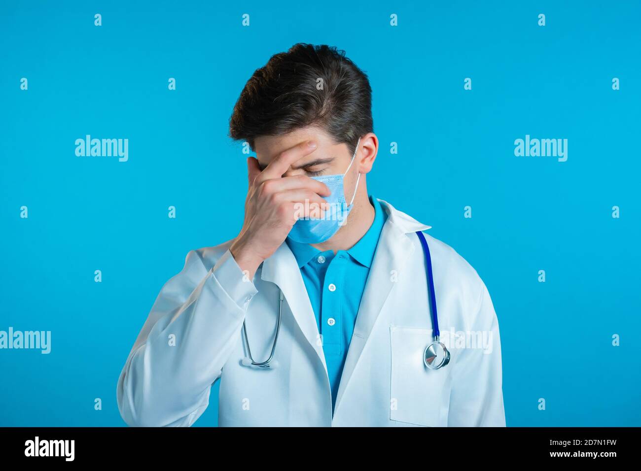 Frustrated doctor man in white wear and mask over blue wall background ...