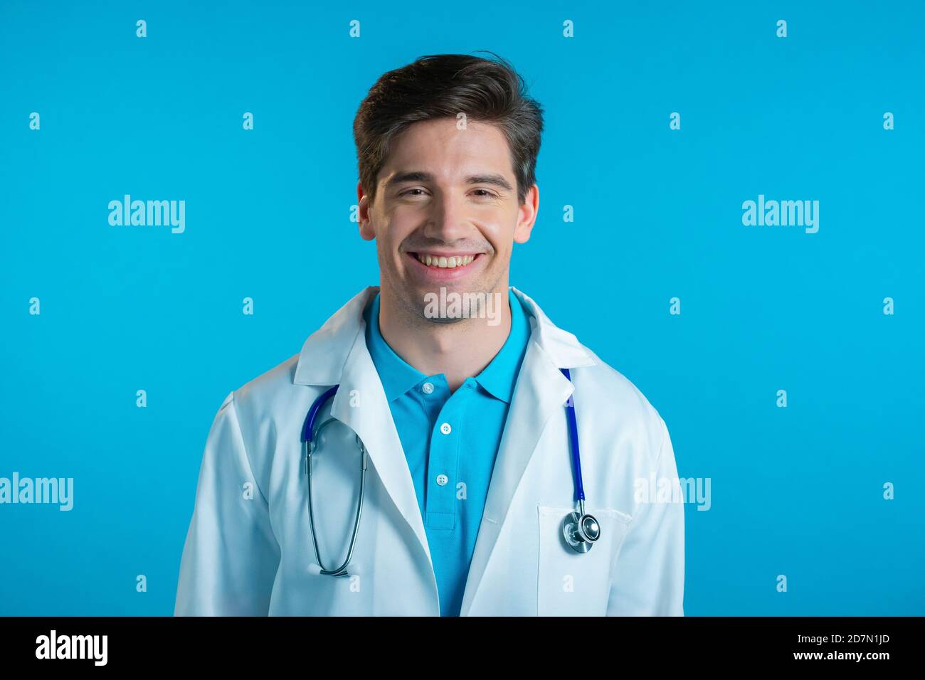 Handsome doctor man in medical wear smiling on blue studio background ...