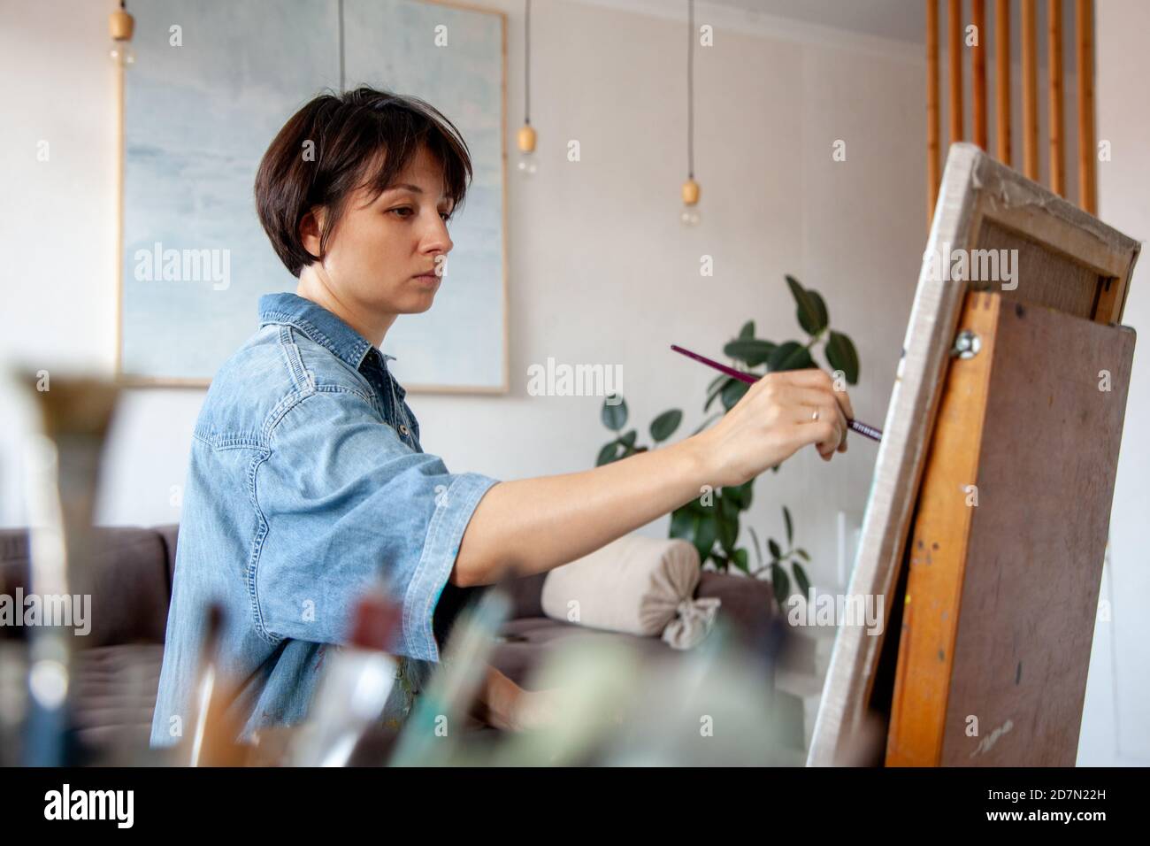 Concentrated short-haired female artist painting on cotton canvas with ...