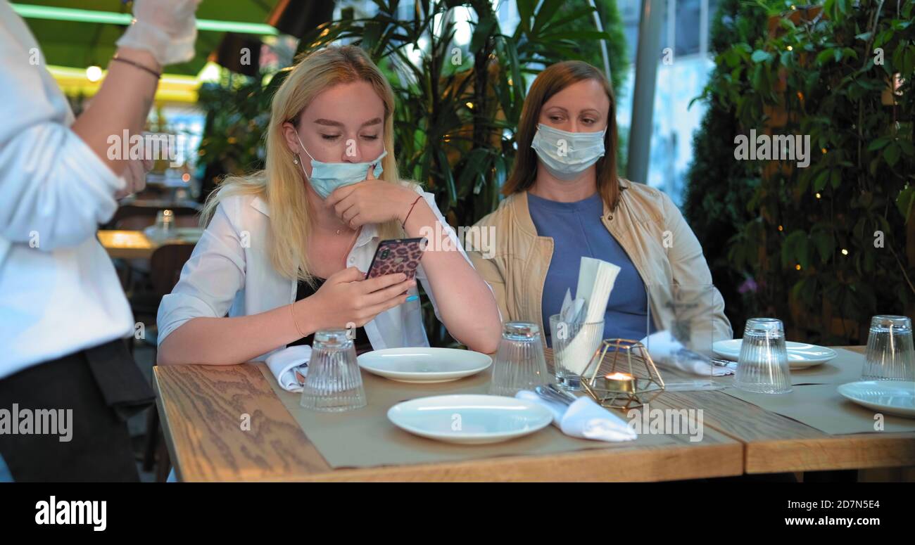 restaurant visitors in sterile face masks look on smartphone display ...