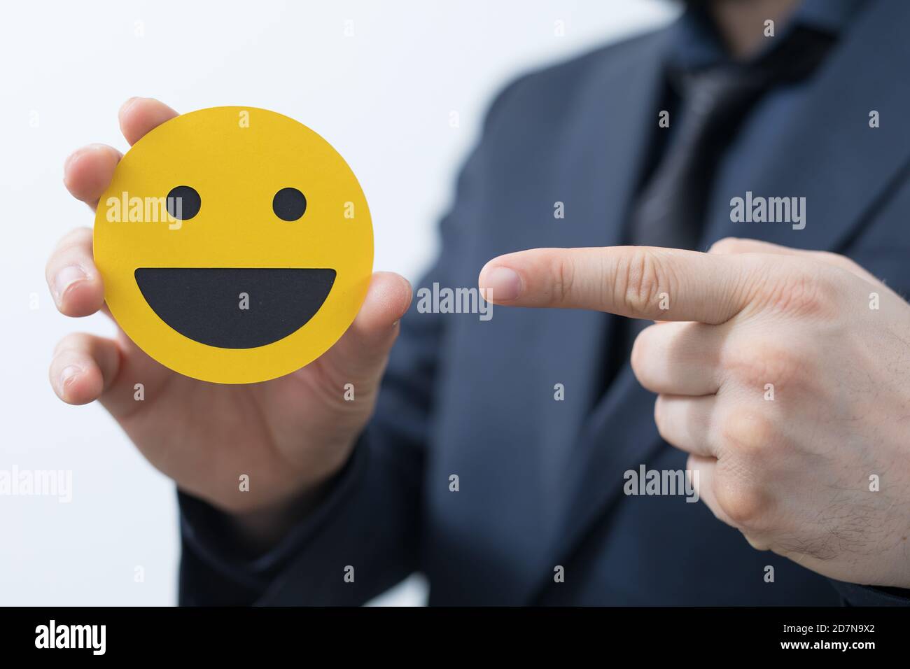 Hand in suit holding a smiley emoji and pointing to it Stock Photo - Alamy