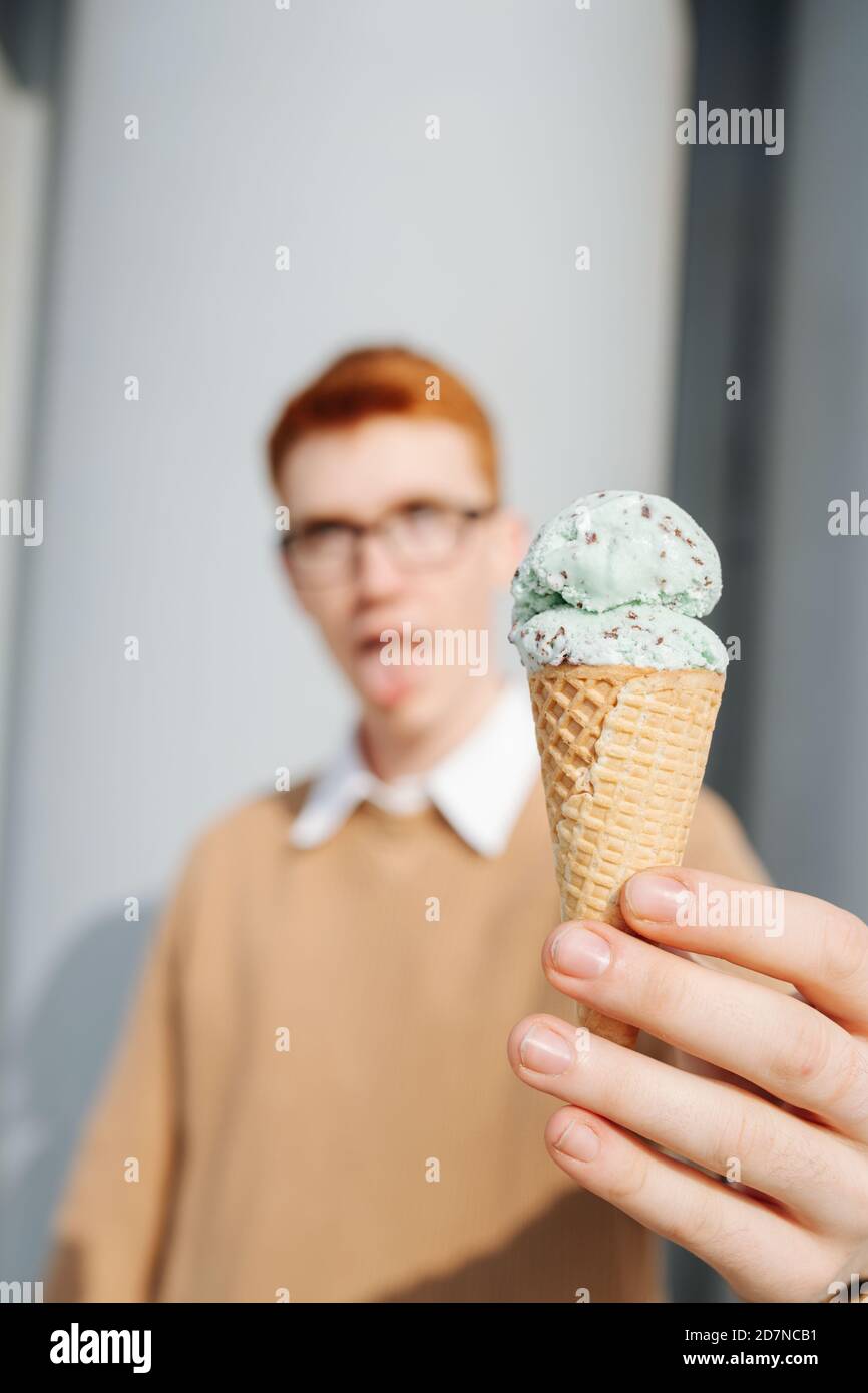 Ice cream cone close to camera held by eccentric young man. Face ...