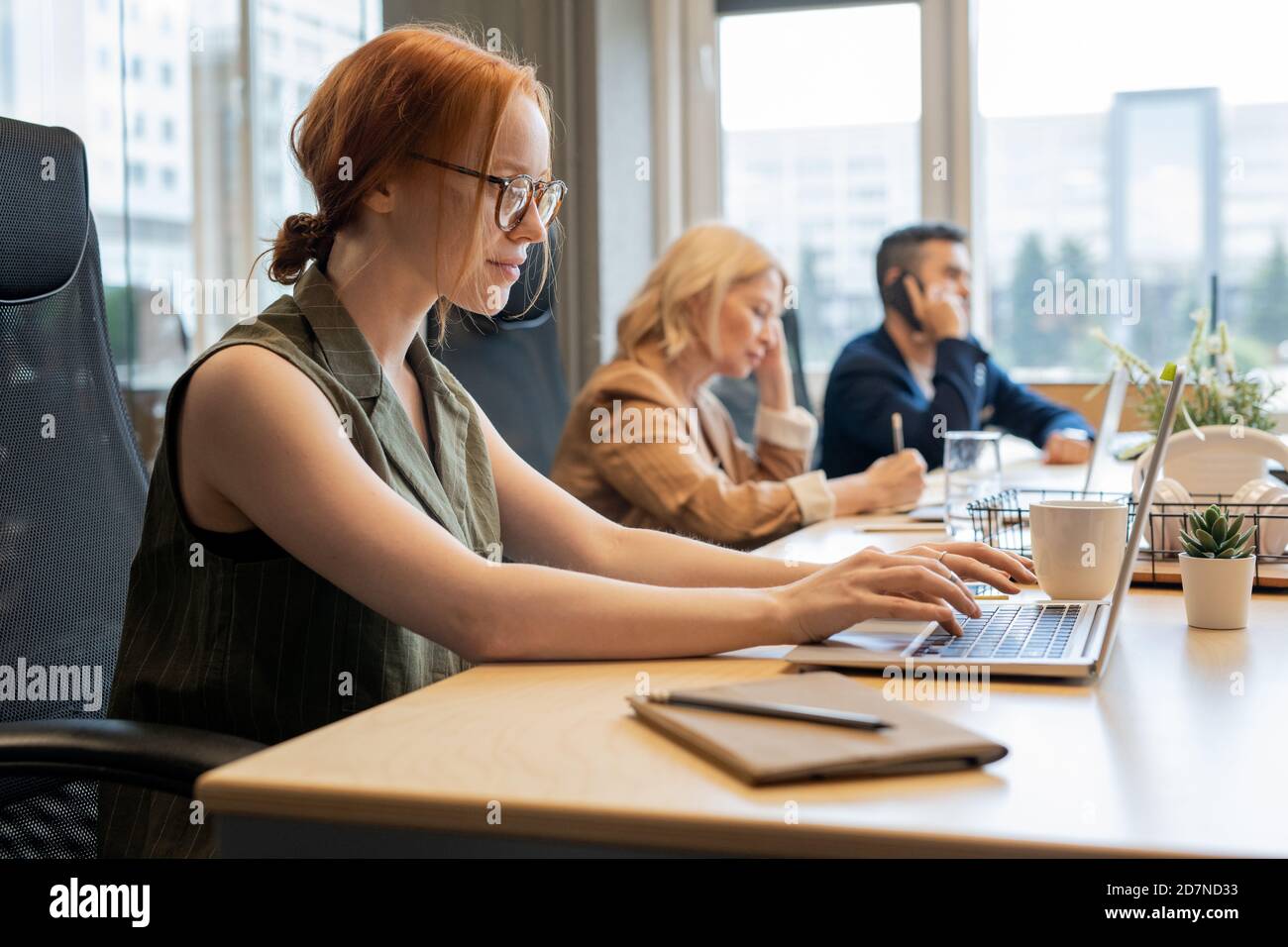 Contemporary young businesswoman and her busy colleagues working ...