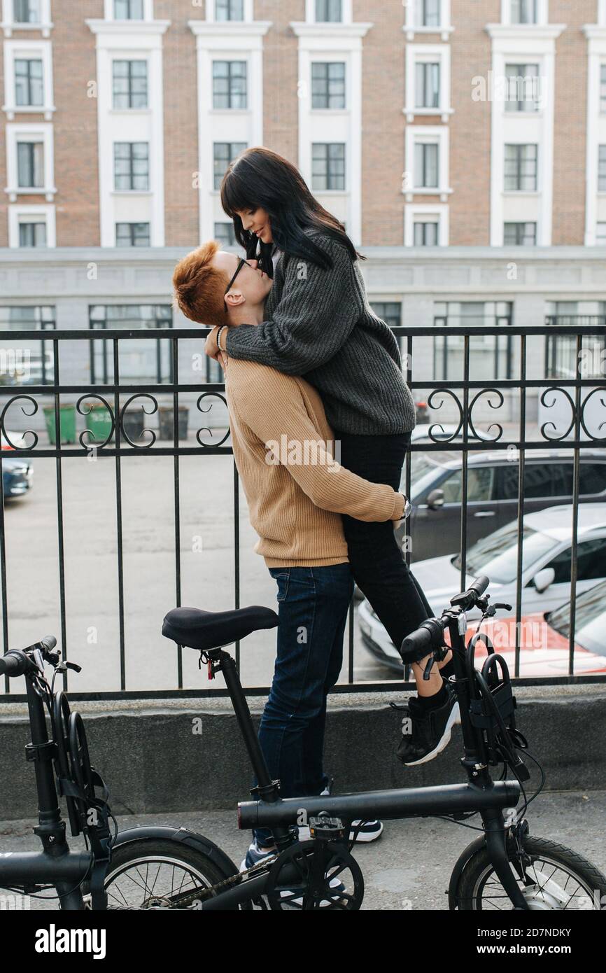 Loving young man holding his girl in the air by her thighs. Side view ...