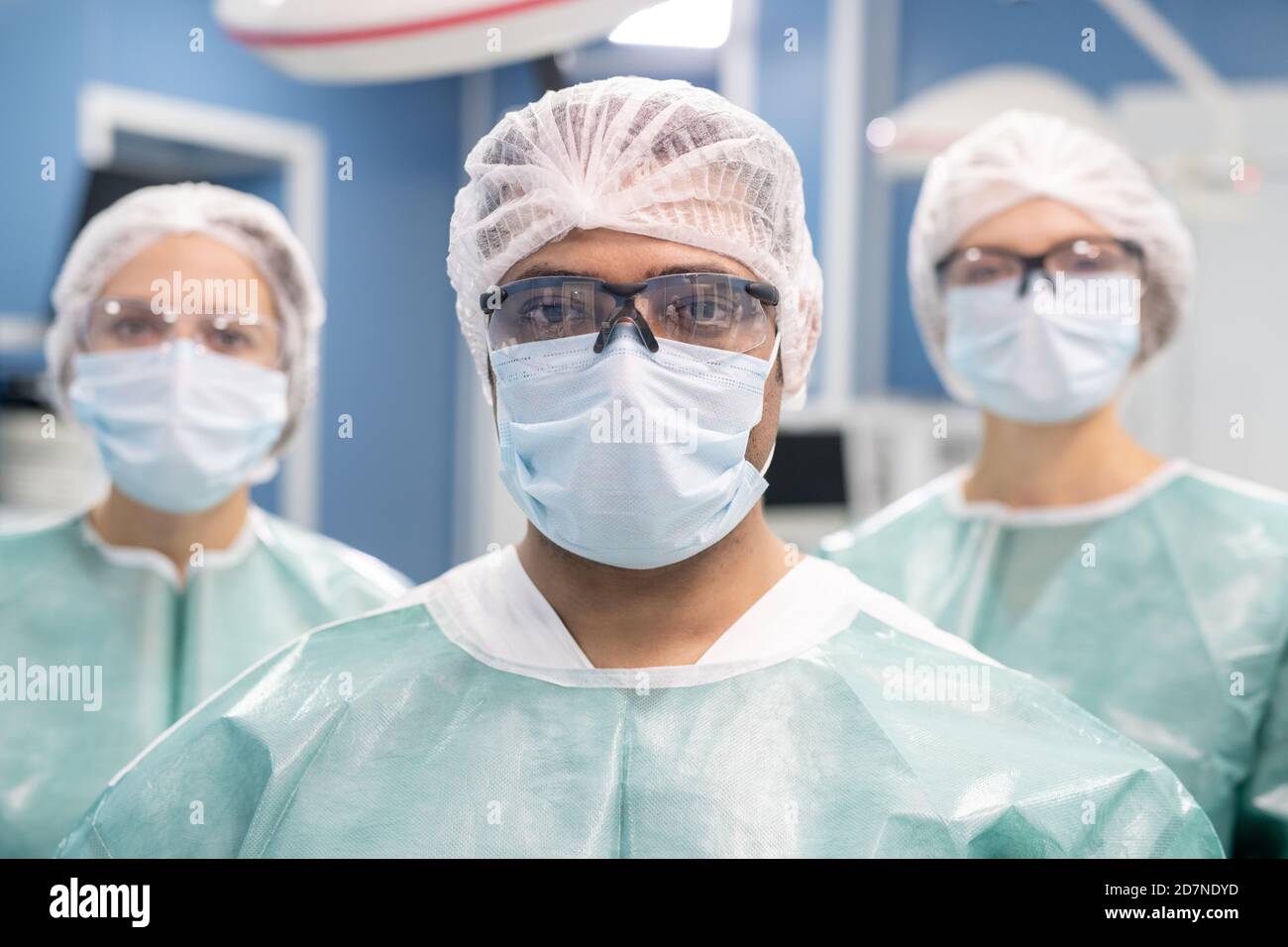 Young professional male surgeon and his two assistants in protective ...