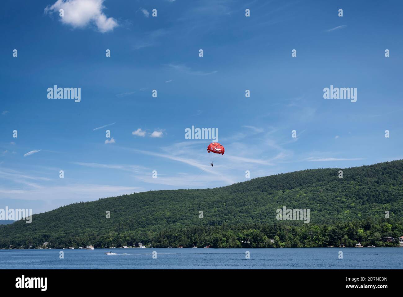 a speedboat pulling a parasail on lake george on a sunny blue sky ...