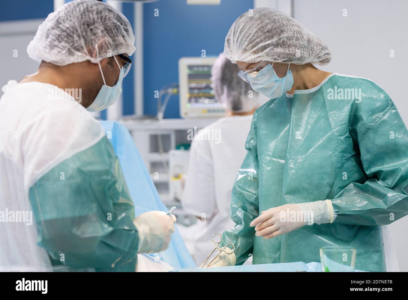 Two surgeons in protective workwear bending over patient during ...
