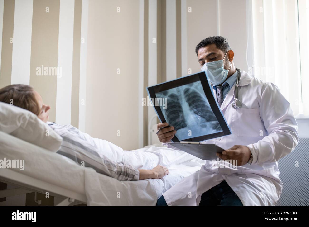 Young radiologist in whitecoat and mask looking at patient lung x-ray ...