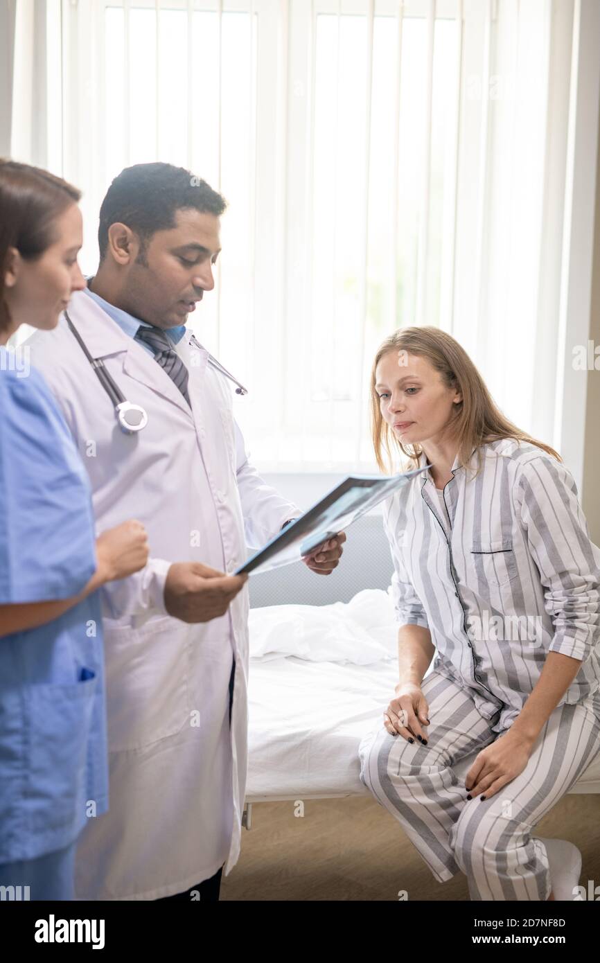 Young sick woman looking at confident radiologist commenting lung x-ray ...