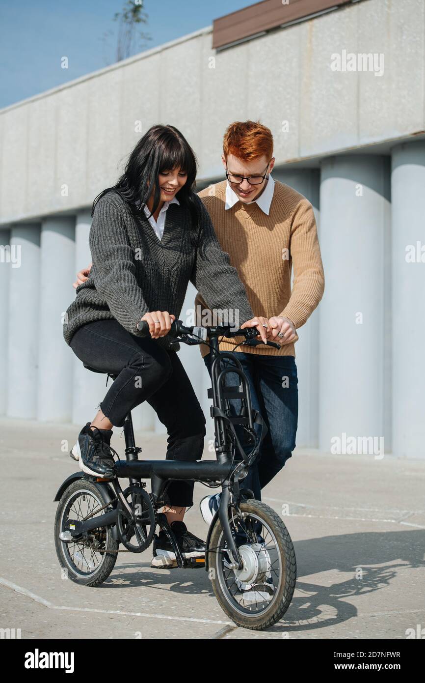 Happy moments. Young man helping girlfriend ride ebike, supporting her ...