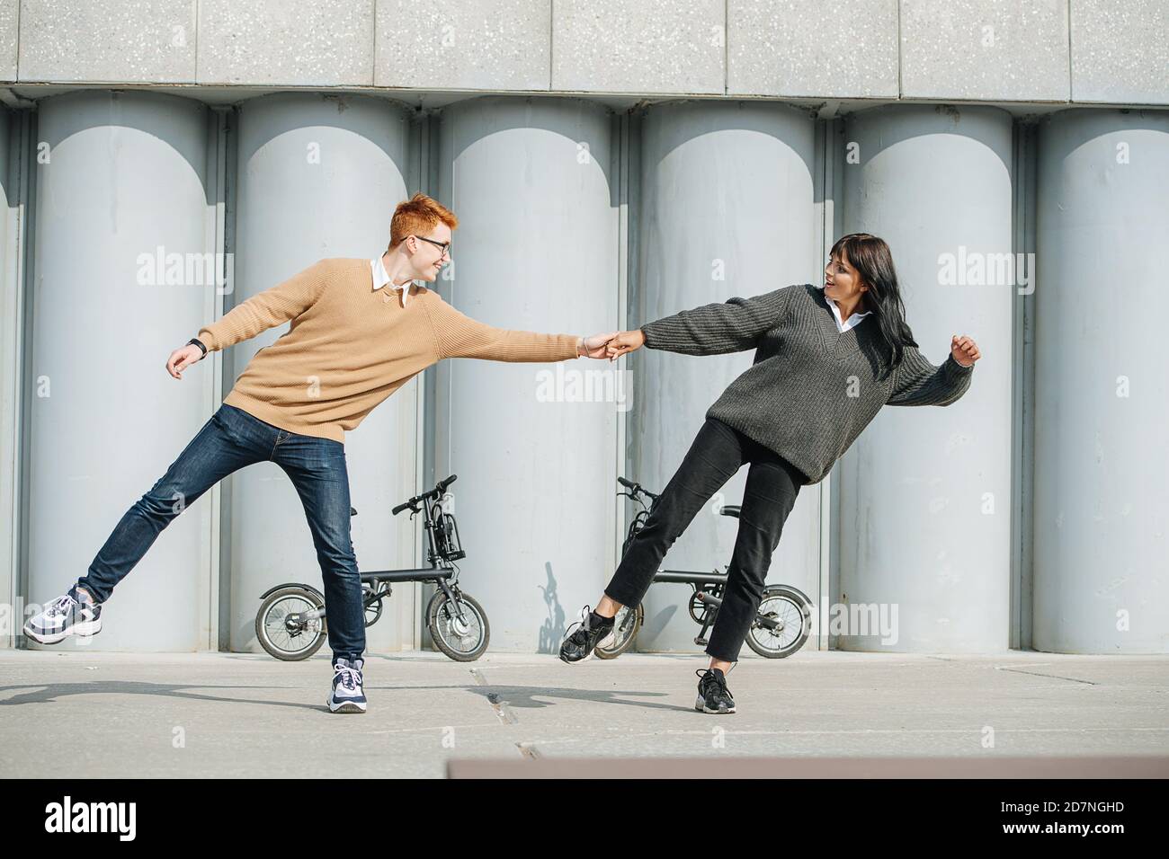 Playful young couple having fun, standing on one foot, pulling one ...