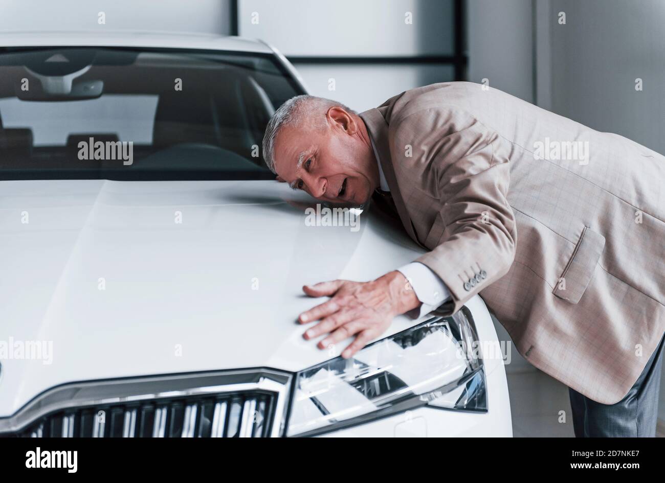 Cheerful aged man in formal wear stands in front of modern white car ...